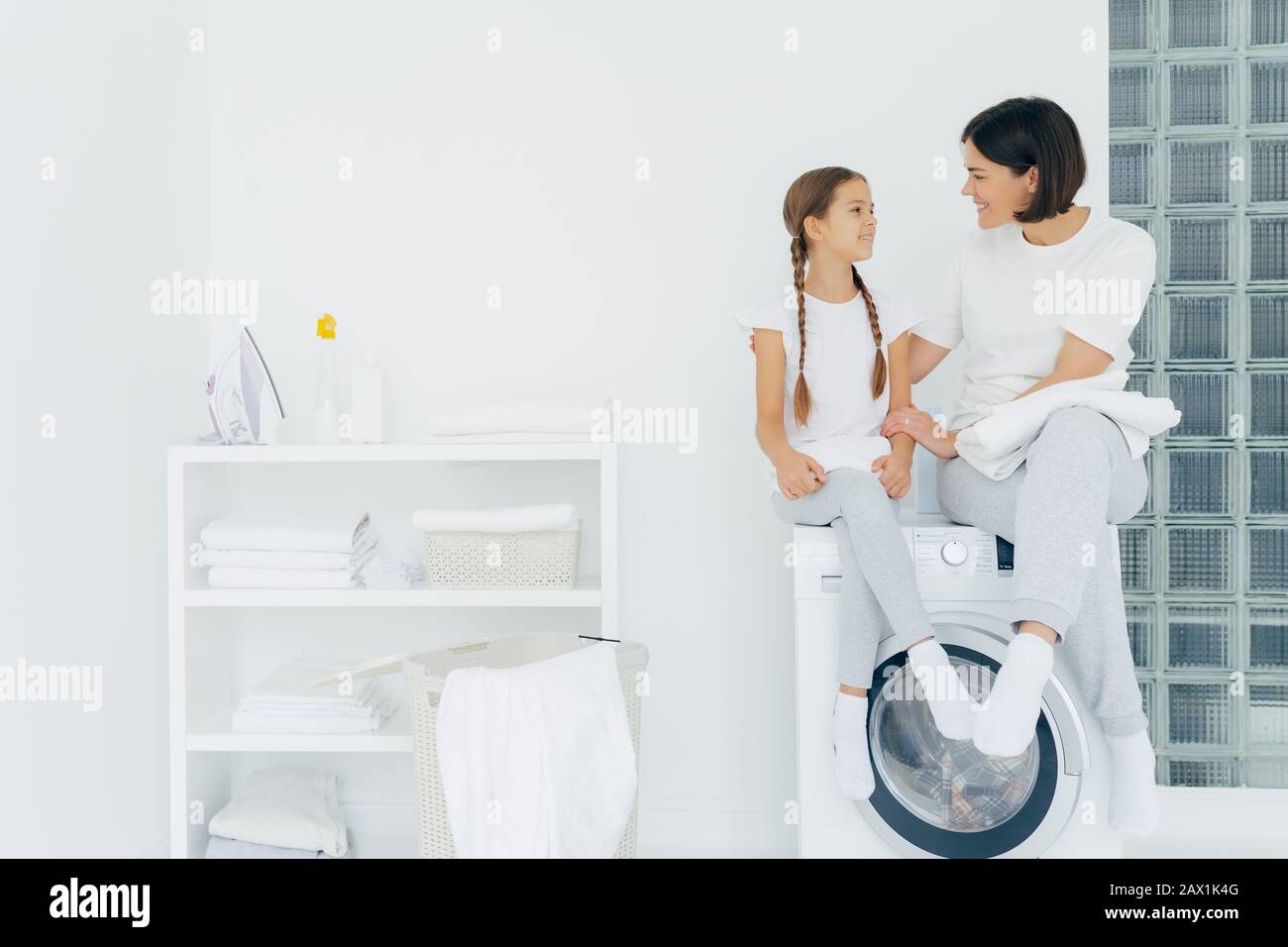 Caring mother talks with daughter, pose on washing machine, surrounded ...