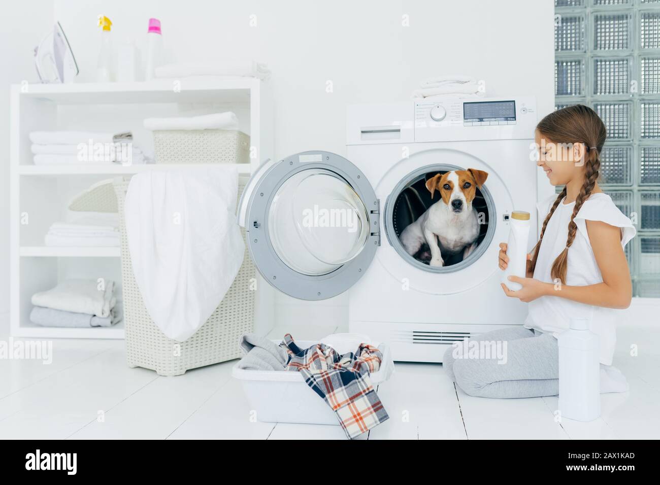 Cheerful little girl stands on knees with washing detergent, poses near ...