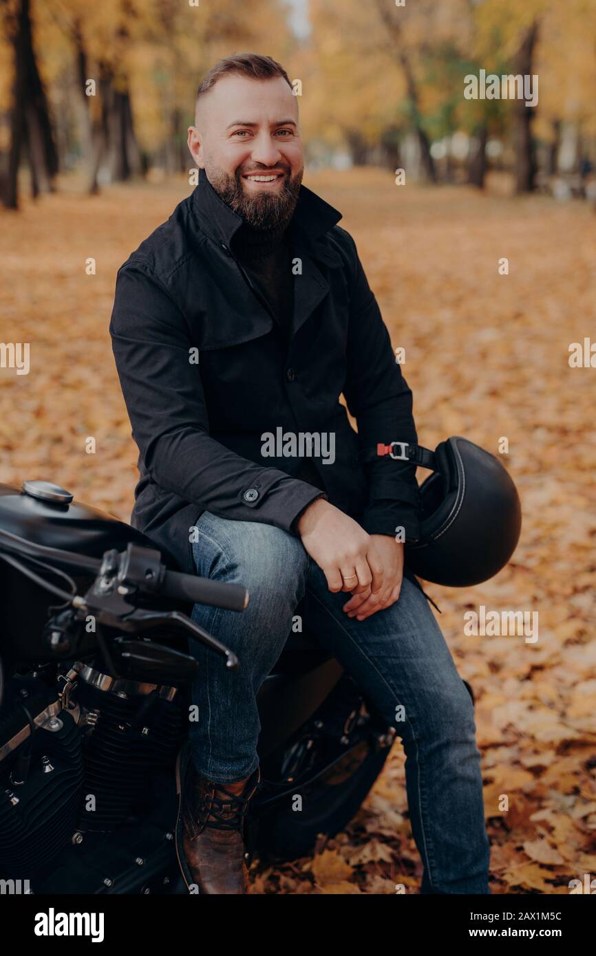 Vertical image of smiling motorcyclist smiles happily, holds helmet ...