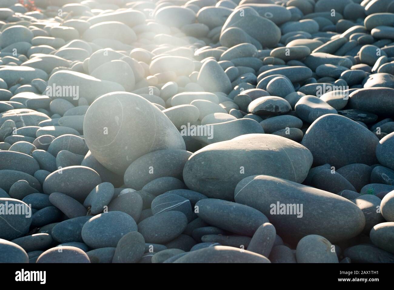 A beam of sunlight shines onto a rock in a collection of pebbles Stock ...
