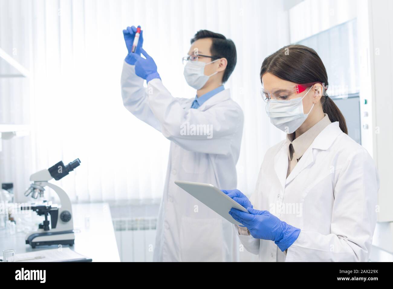 Two young scientists wearing protective masks and gloves working on new ...