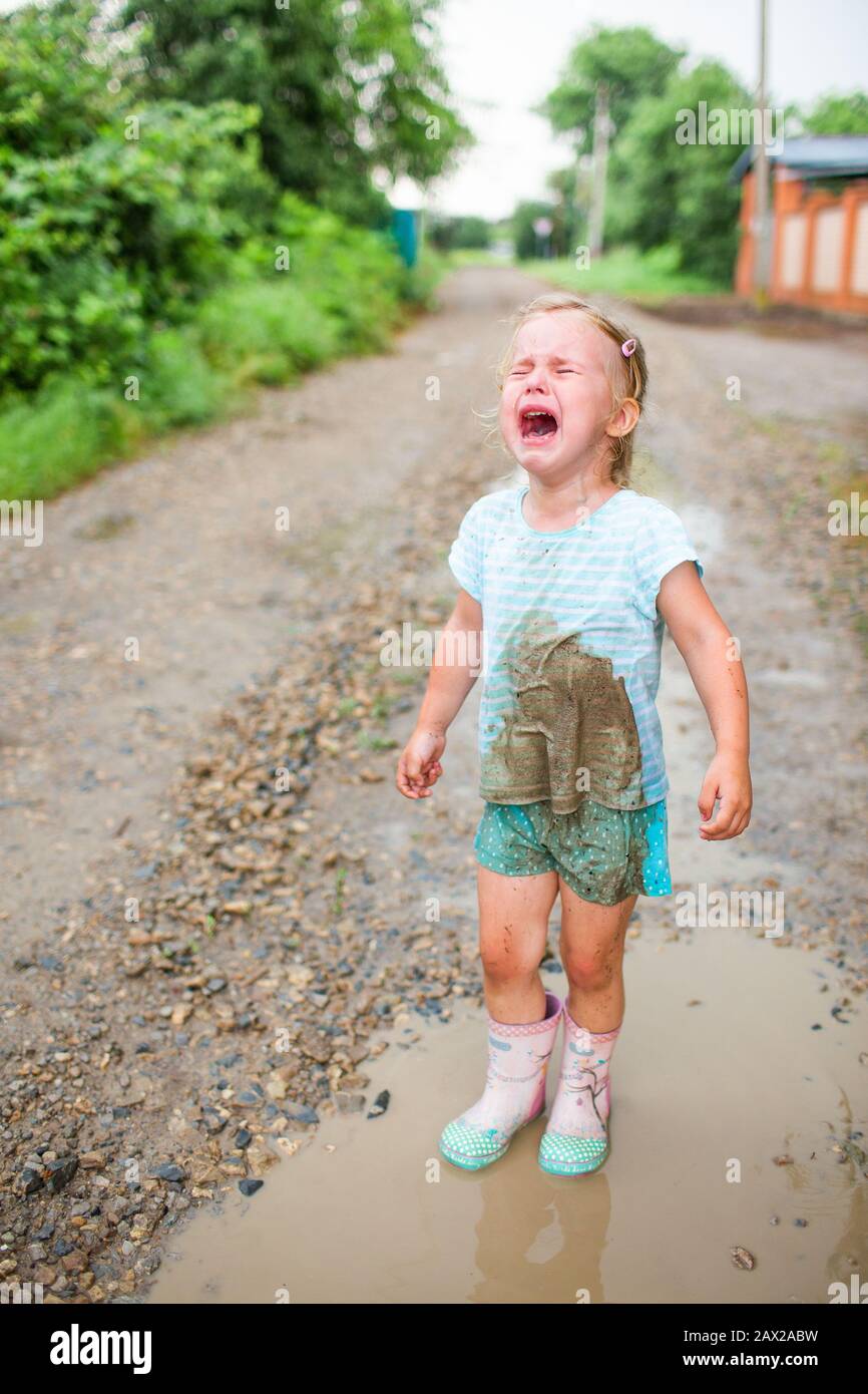 Little blonde girl crying in her dirty clothes after fall into a puddle ...