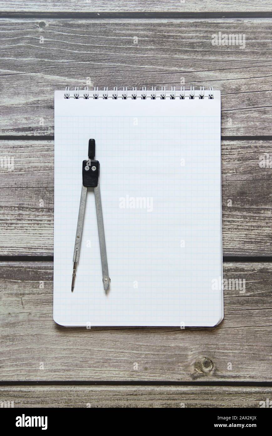 Notepad with a blank white sheet in a checker paper with compass lies ...