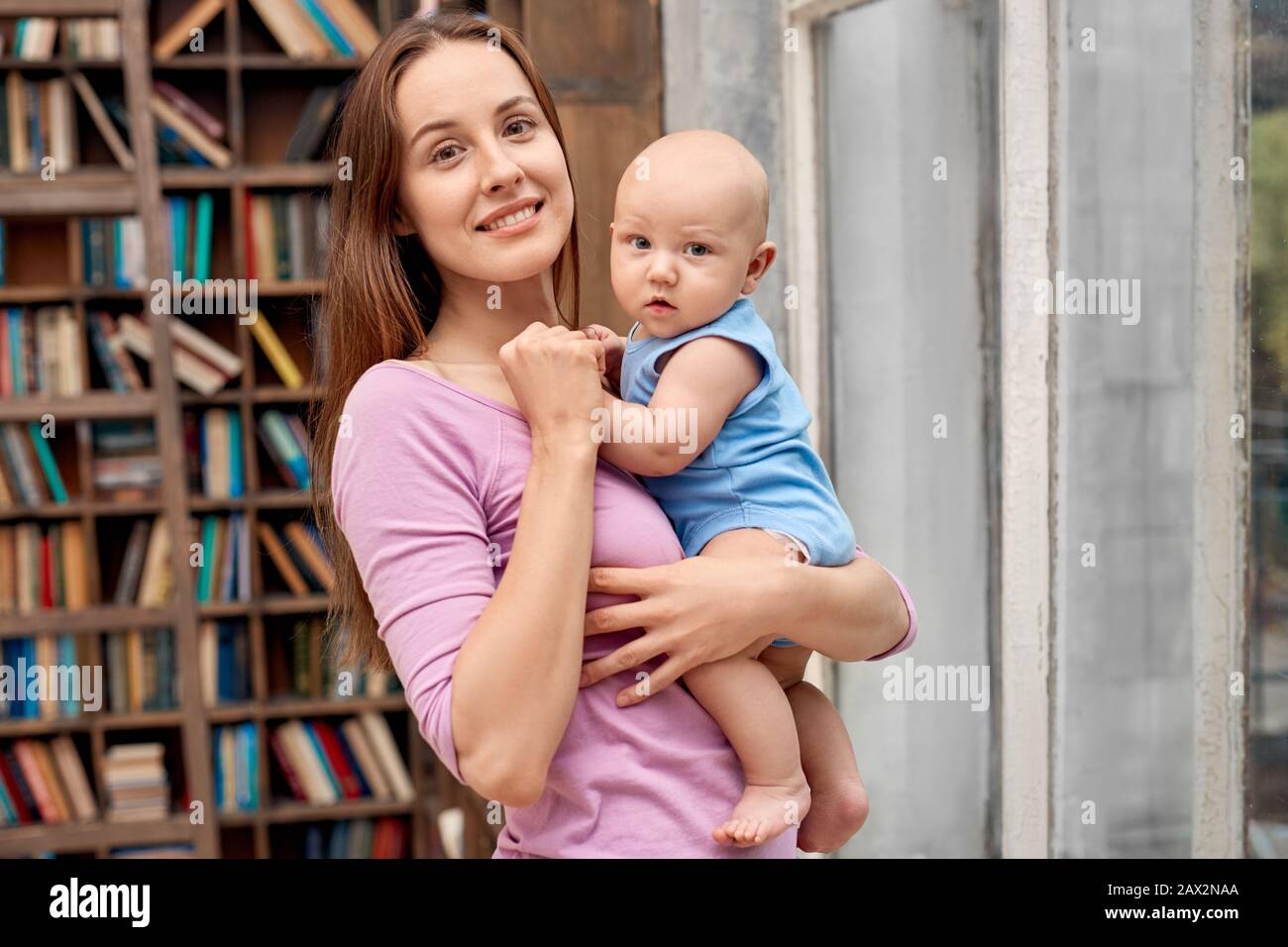 Baby Care. Young mother standing holding little son at home posing to camera cheerful holding ...