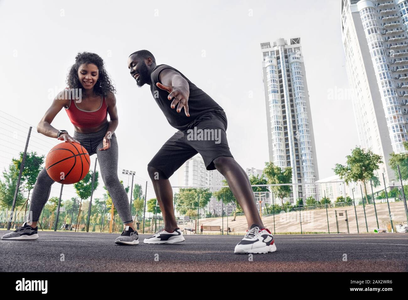 Outdoors Activity. African couple on basketball court girl dribbling ...