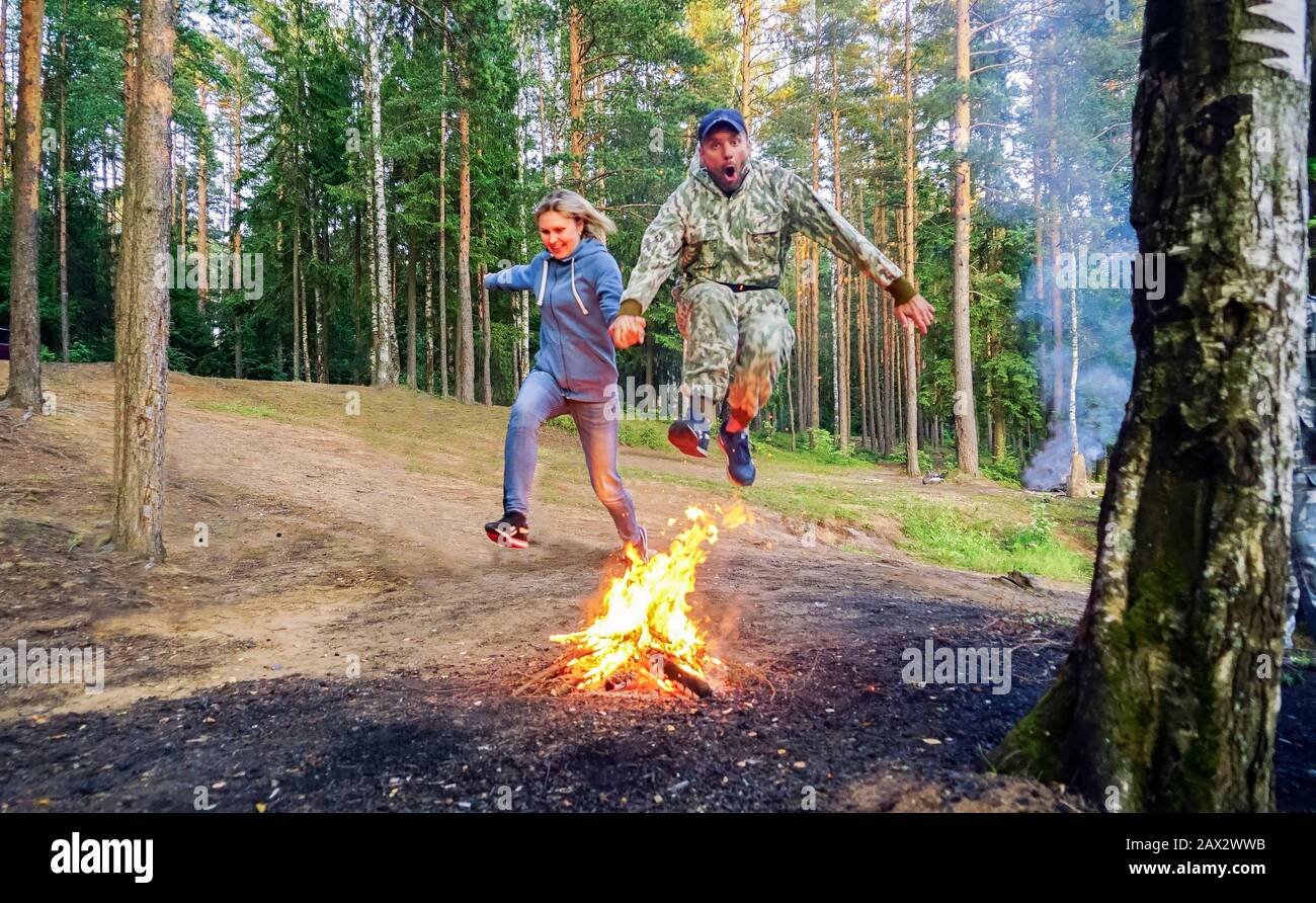 Young man and woman in a jump over a burning fire on the lake shore ...