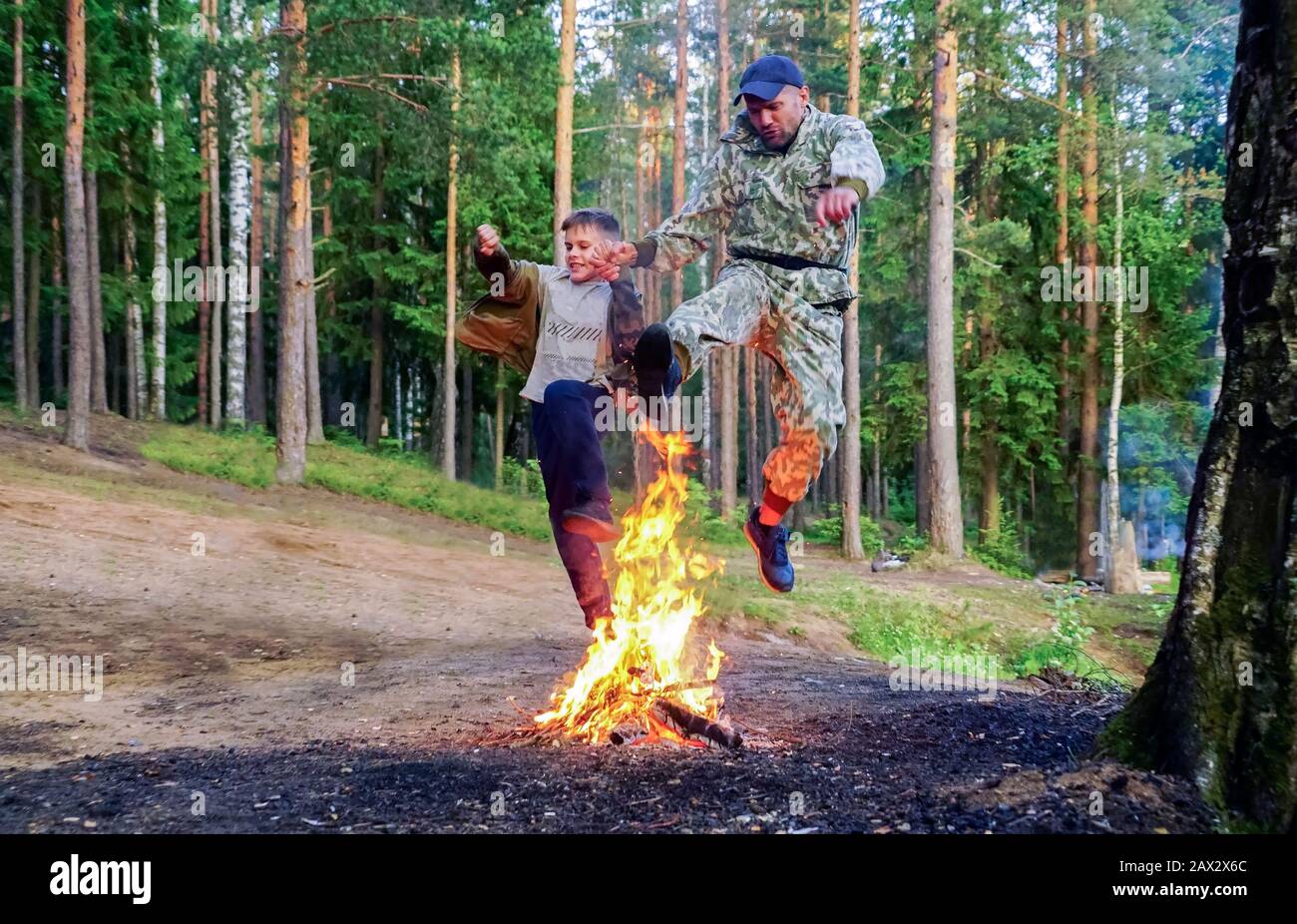 Father and son in a jump over a burning fire on the lake shore Stock ...