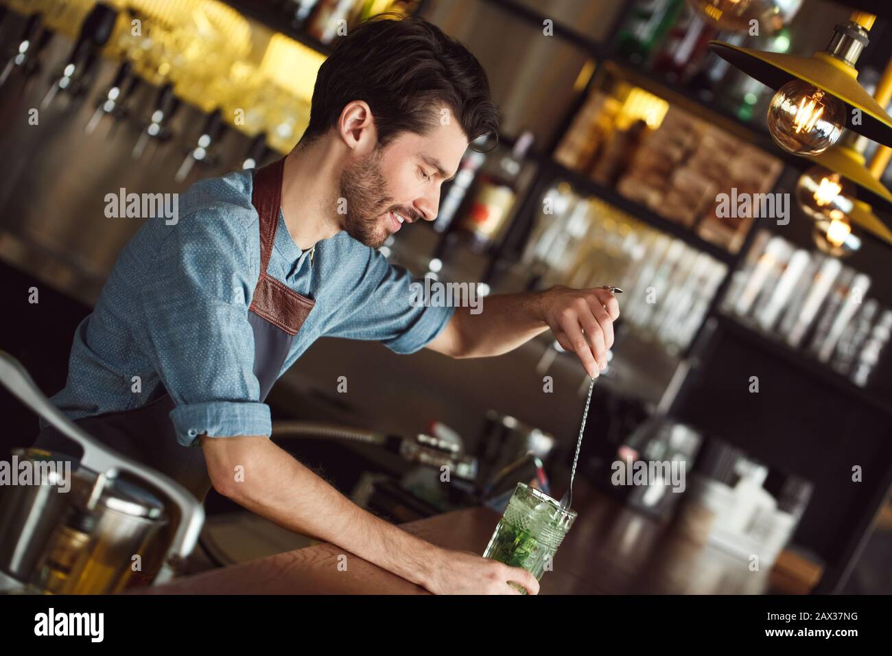 Making Drink. Bartender standing at counter mixing mojito smiling cheerful Stock Photo - Alamy