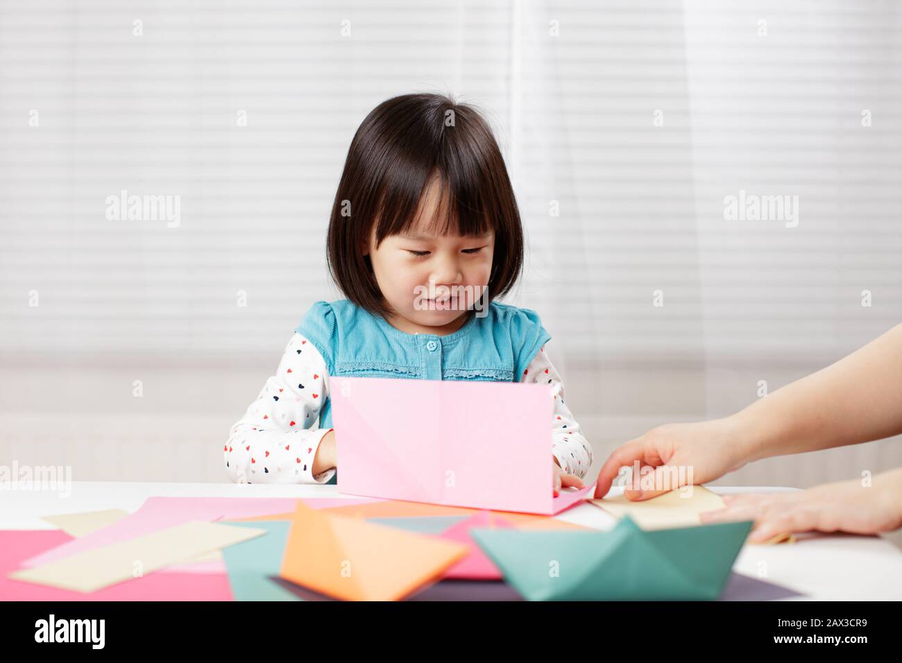 toddler girl learn making Origami at home against white background ...