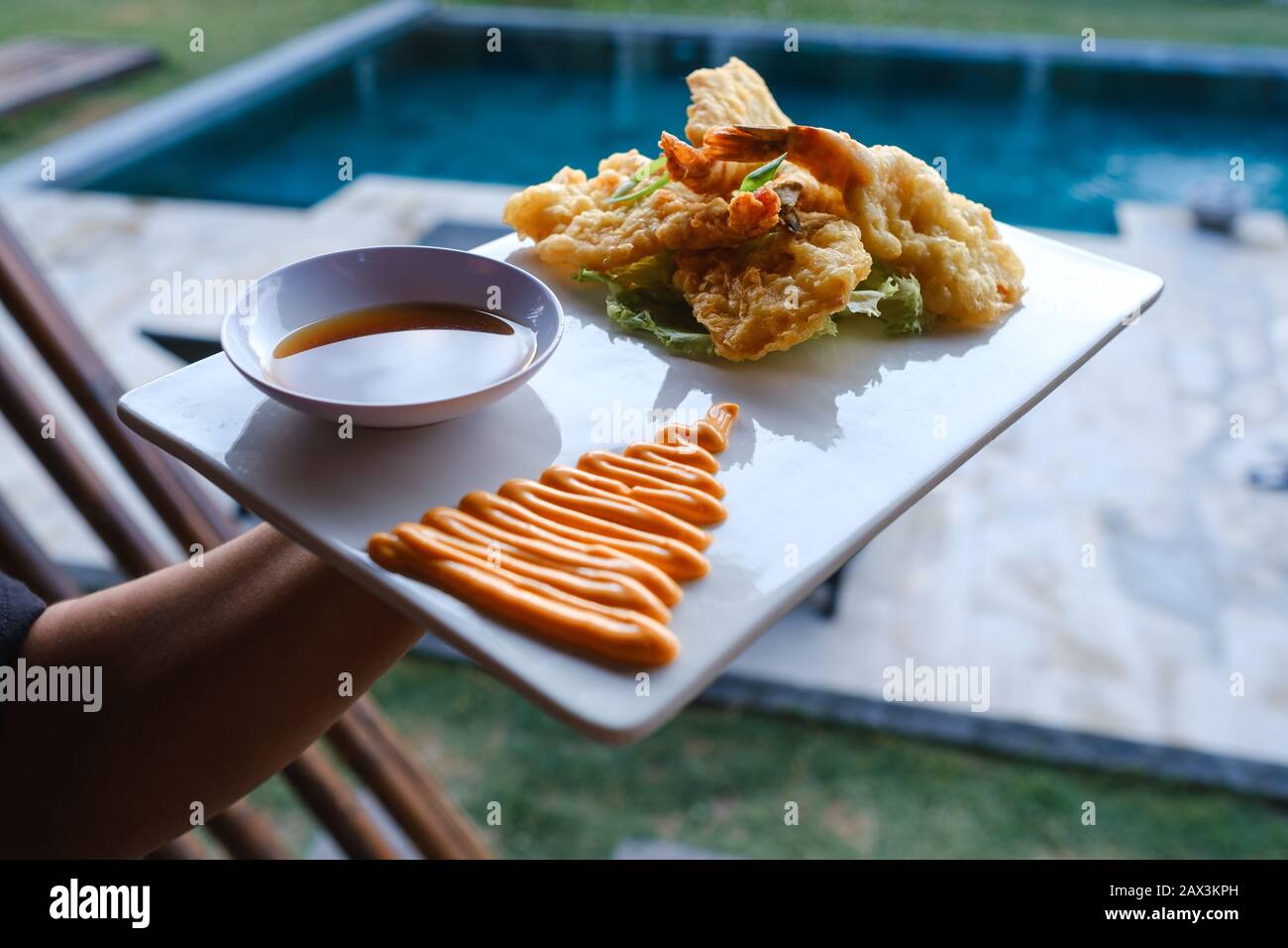 Wide angle shot of someone holding a tray of food in front of the pool ...
