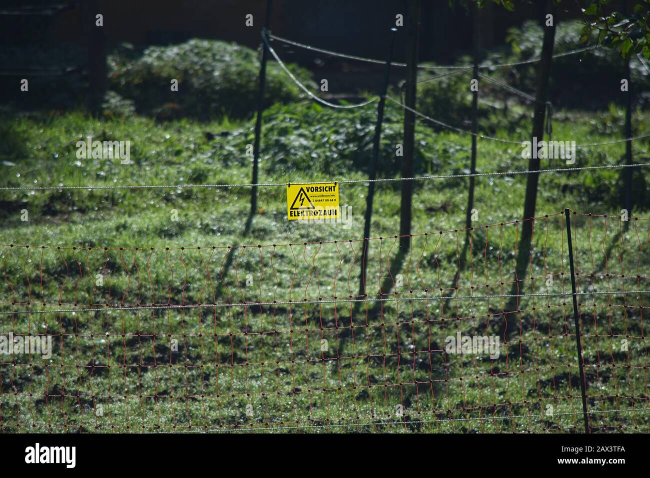 Yellow hazard warning sign on an electric fence hanging from a strand ...