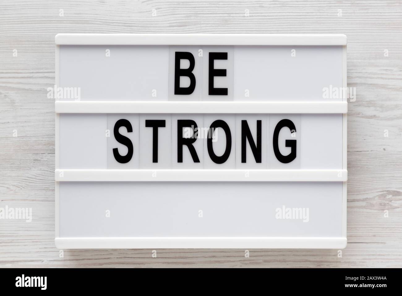 'Be strong' words on a lightbox on a white wooden surface, top view ...