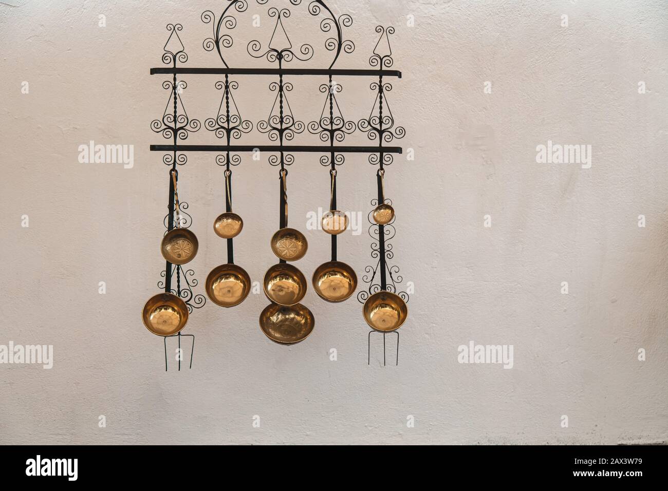 Hanger with old golden ladles hanging from it under the lights against ...