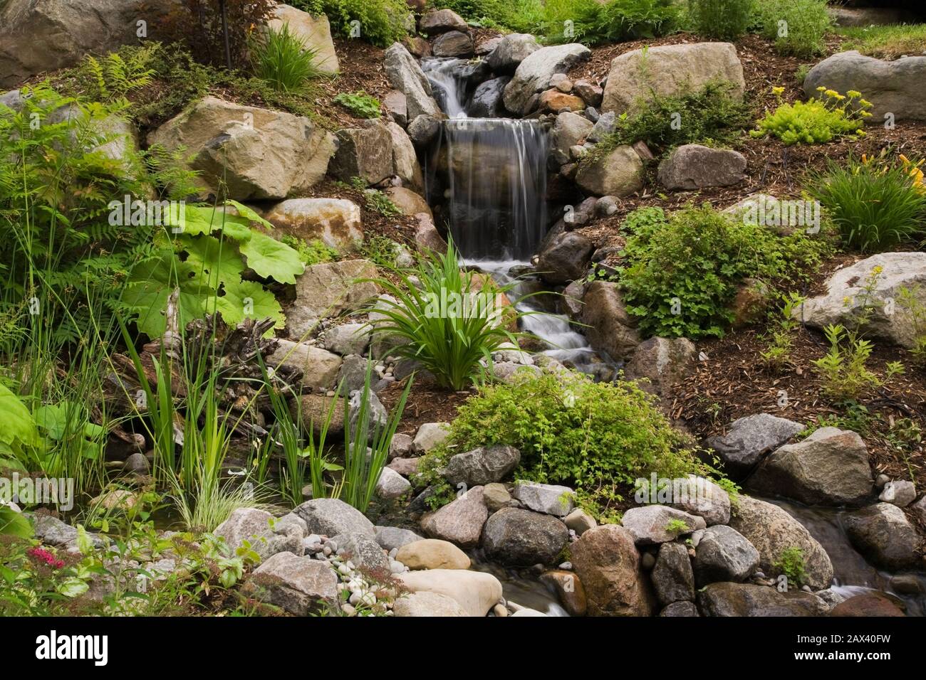 Cascading waterfall through rock edged borders planted with perennial ...