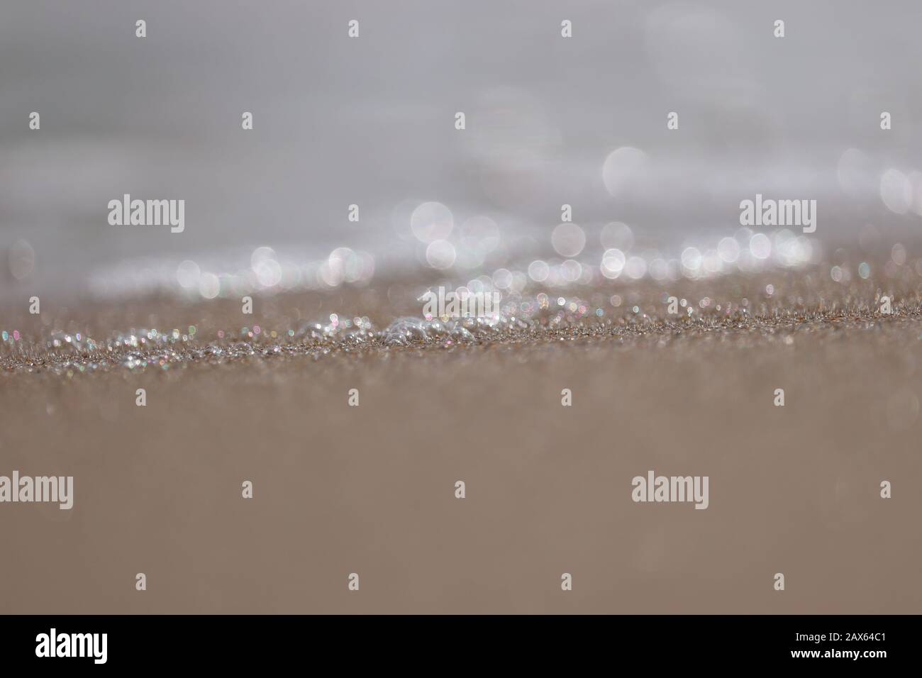 close up shot of water line with bubbles and sandy beach background ...