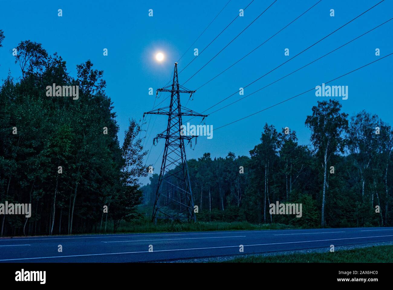 Bright moon over the high voltage transmission line. Empty night road ...