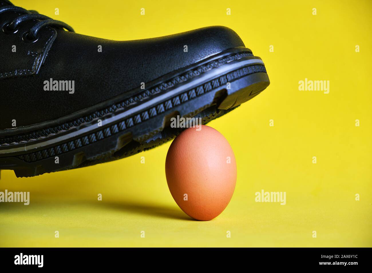Black boot on a yellow background stepped on a fragile chicken egg ...