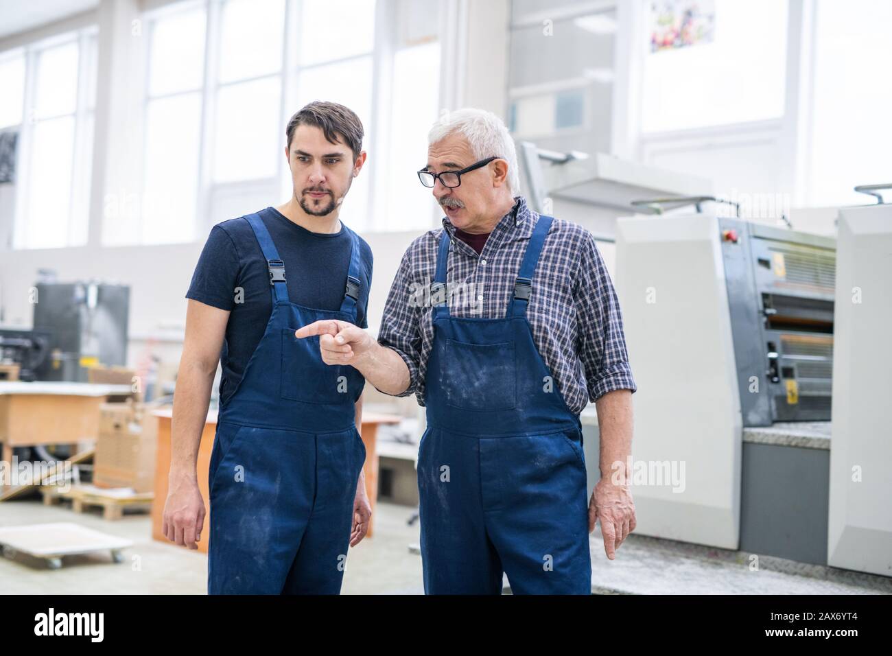 Senior foreman in glasses pointing with finger and giving task to young ...