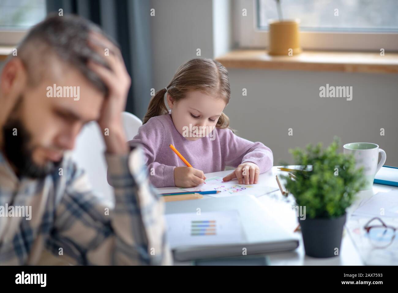 Little girl drawing at the table and tired dad Stock Photo - Alamy