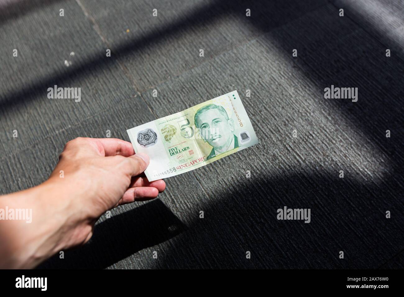 A hand pick up a five dollar Singapore money banknote on the floor ...