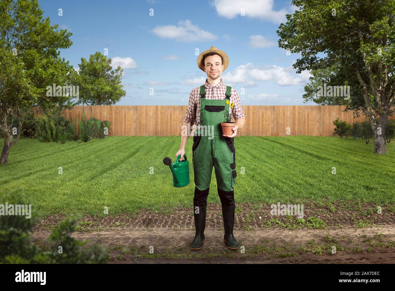 Happy gardener with a watering can and a flower pot standing in a green ...