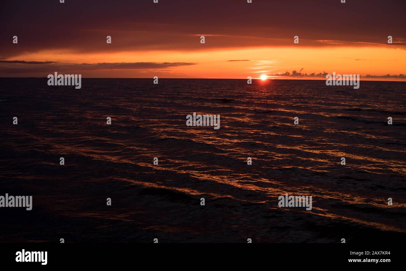 Sun sets into the sea with dark cloud over it and light reflections on ...