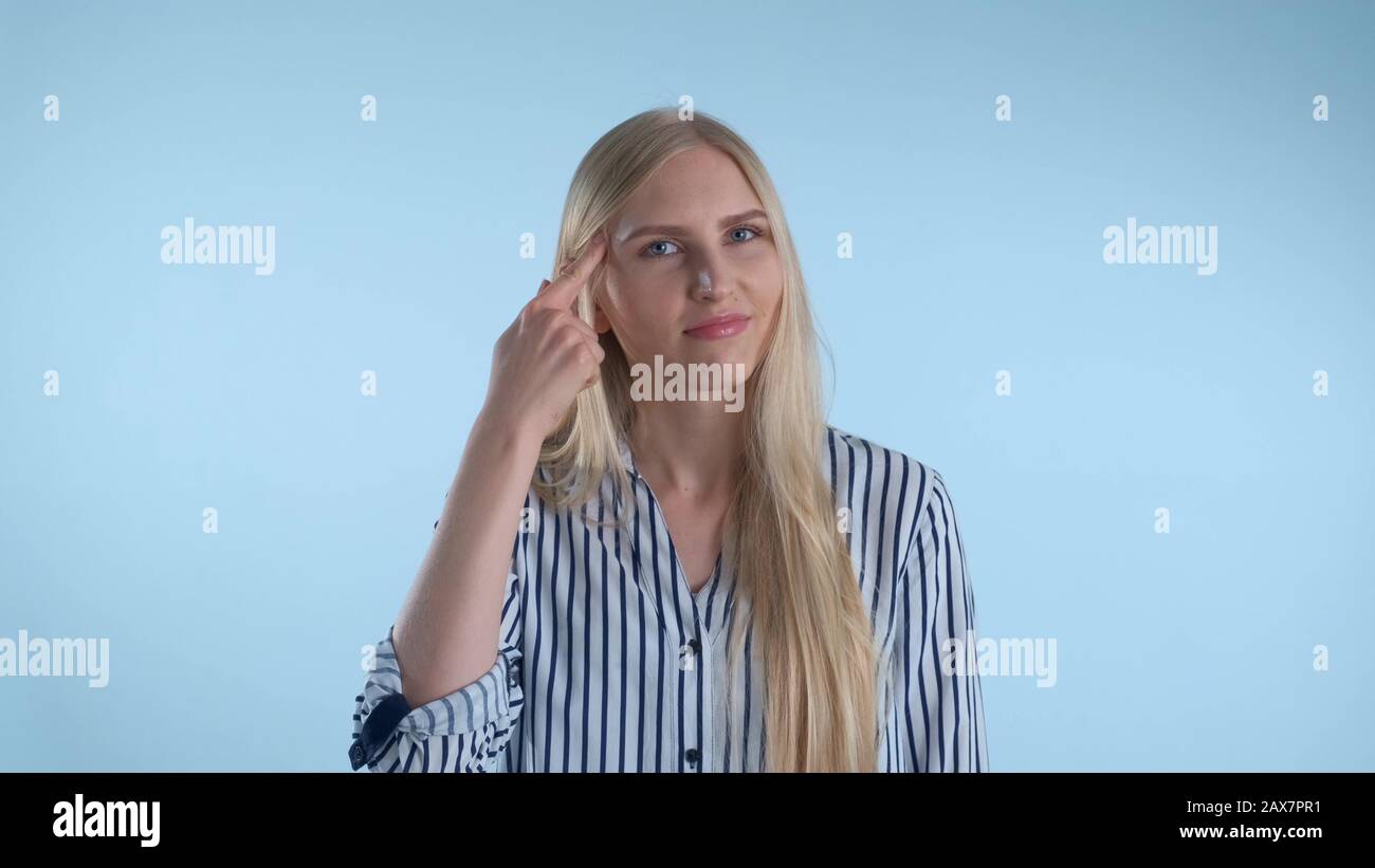 Attractive woman twisting her index finger at temple on blue background ...