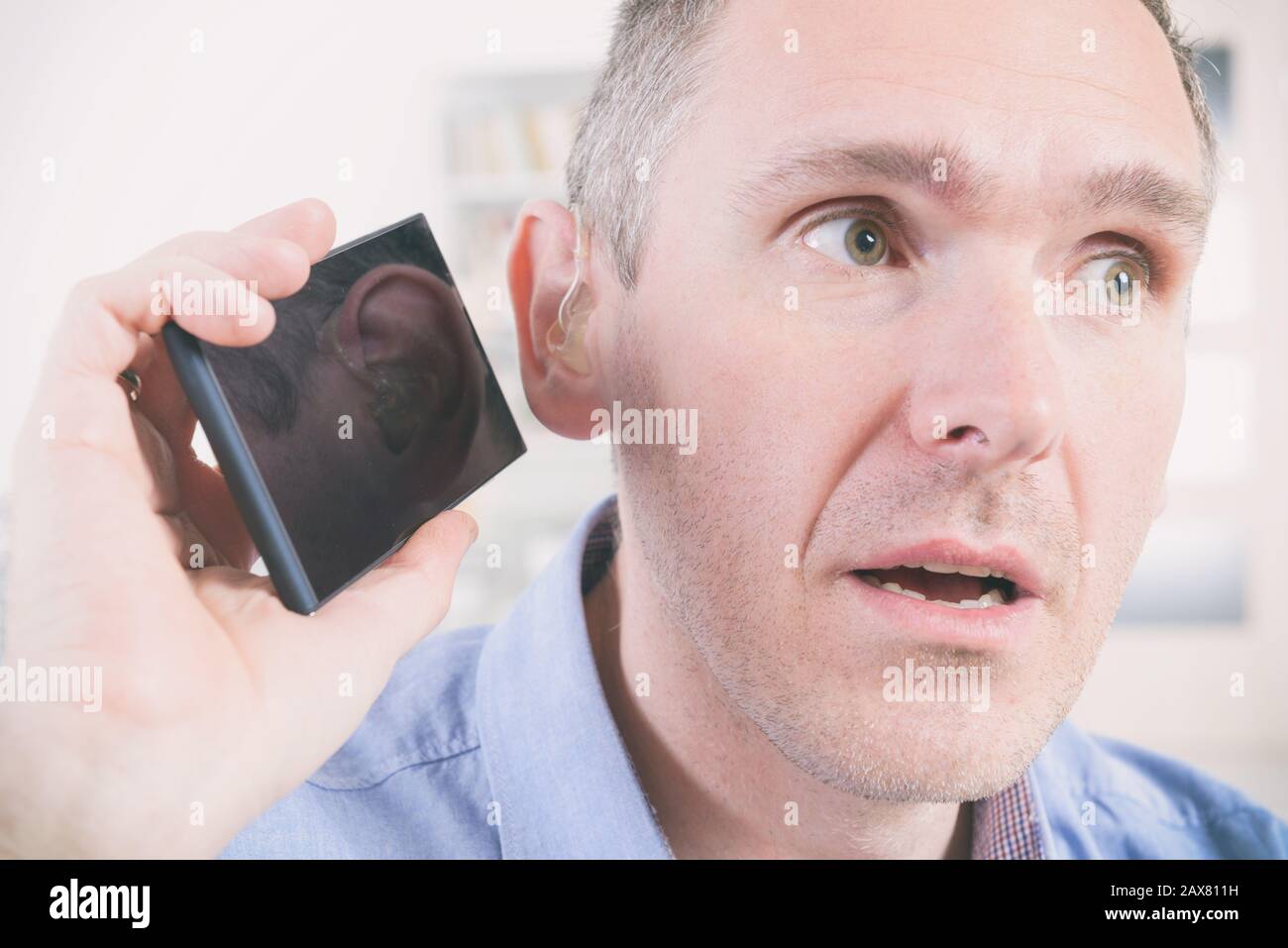 Man wearing deaf aid in ear is attempting to use smart phone Stock ...