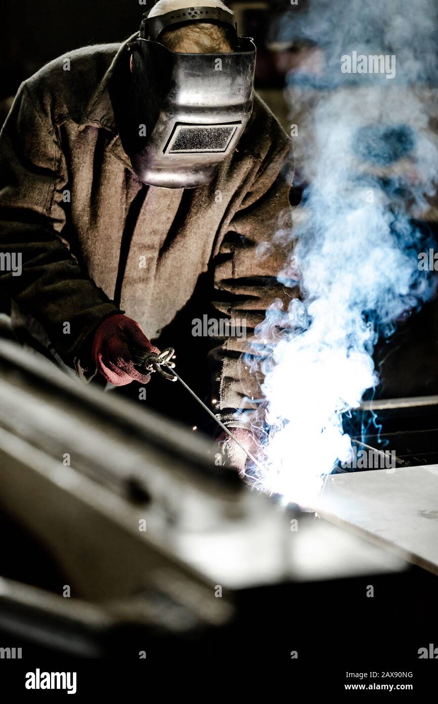 worker in protective uniform and mask welding metal. man using electric ...