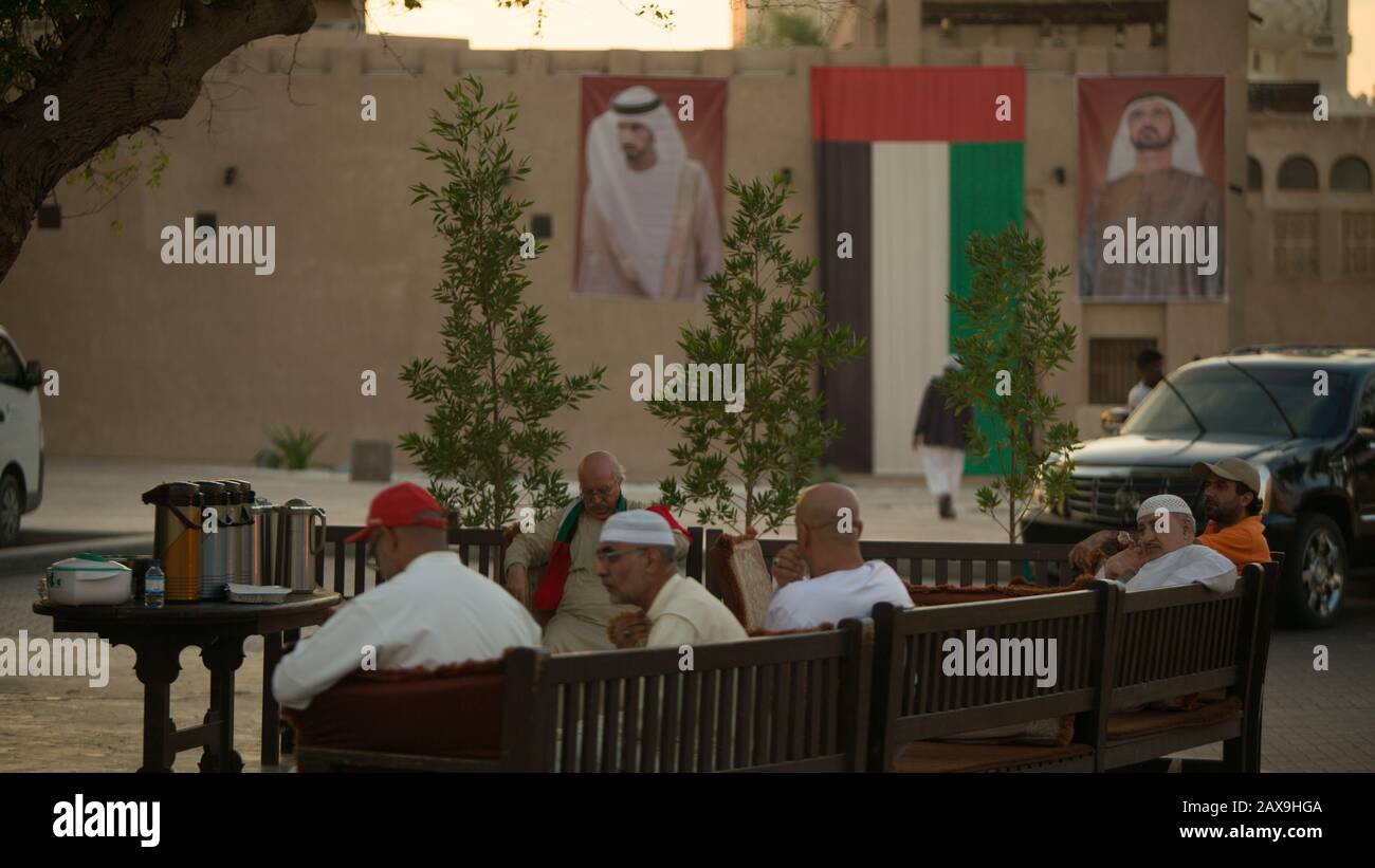 Men sitting in front of a building with UAE Flag and posters of sheik ...