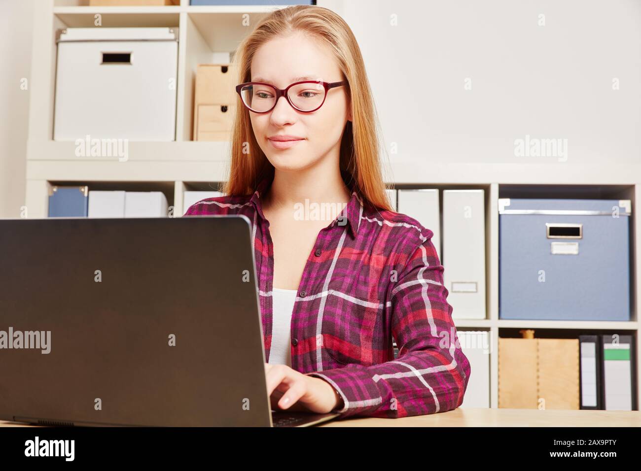 Young woman with glasses working on laptop computer in the office Stock ...