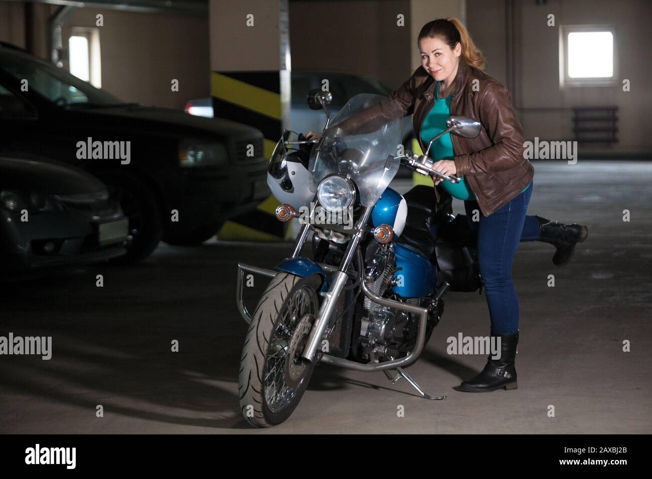 Motorcyclist woman getting behind a wheel of her bike in garage, dark ...