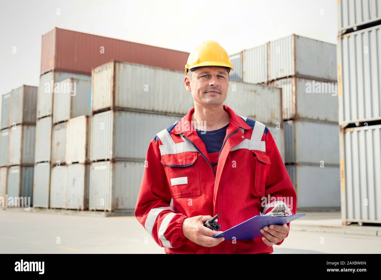 Portrait confident dock worker with clipboard and walkie-talkie at ...
