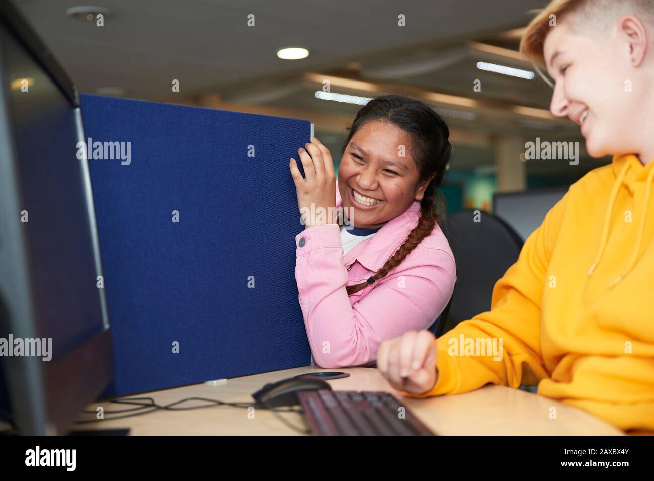 Happy young female college students laughing at computer in library ...
