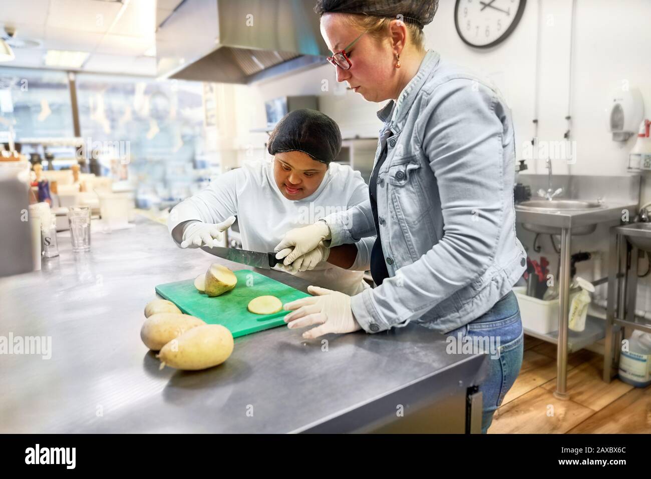 Chef and young woman with Down Syndrome cutting potatoes in cafe Stock ...