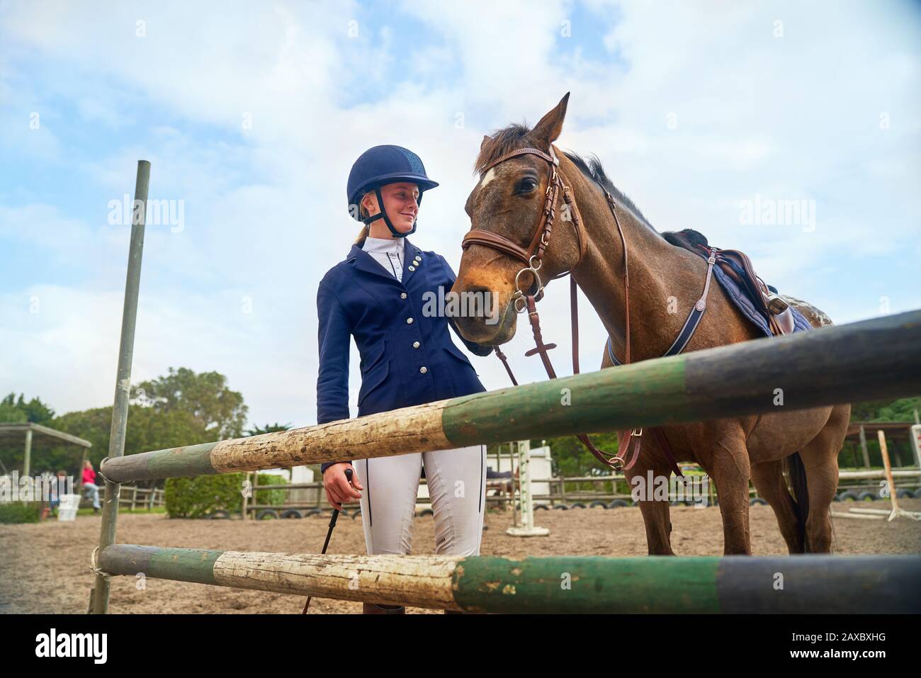 Teenage girl in equestrian helmet with horse at obstacle in paddock ...