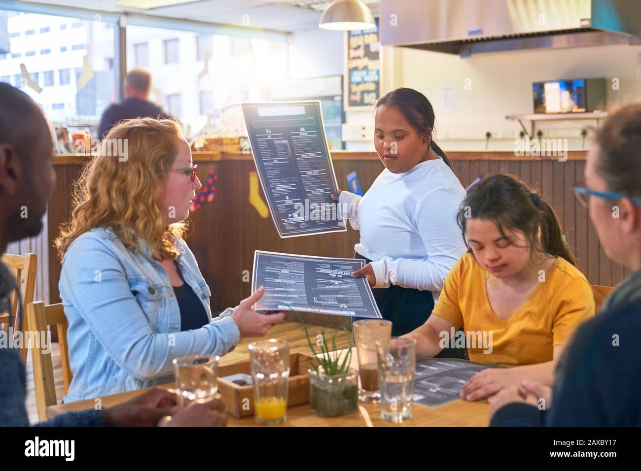 Young female server Down Syndrome giving menus to customers in cafe ...