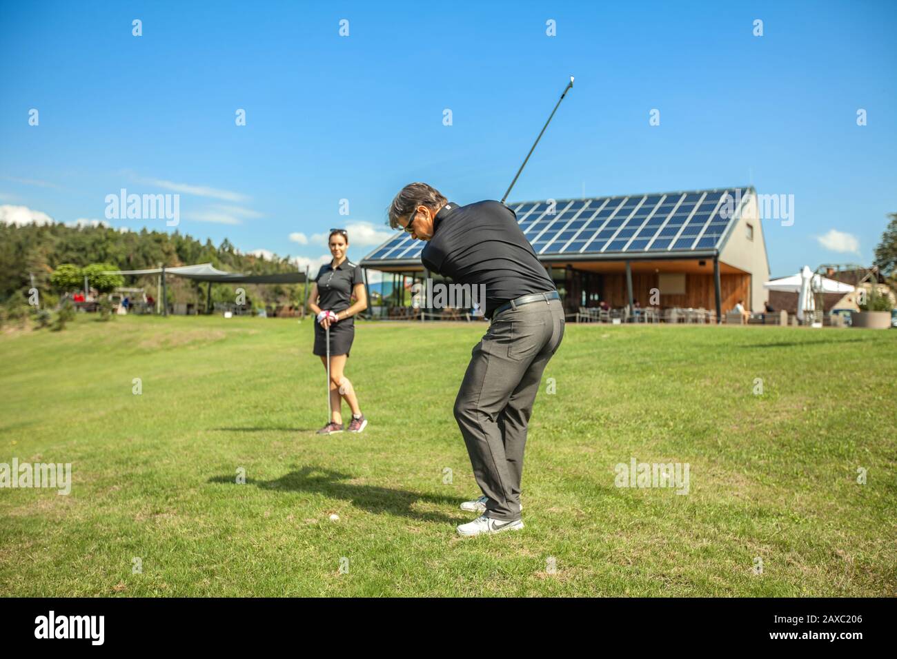 Stunning shot of a male golfer swinging a golf club with his wife ...
