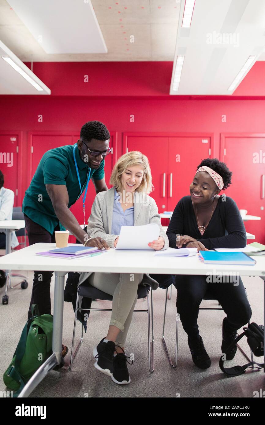 Community college instructor helping students at desk in classroom ...