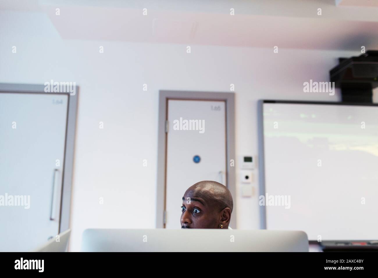 Surprised male community college student using computer in classroom ...