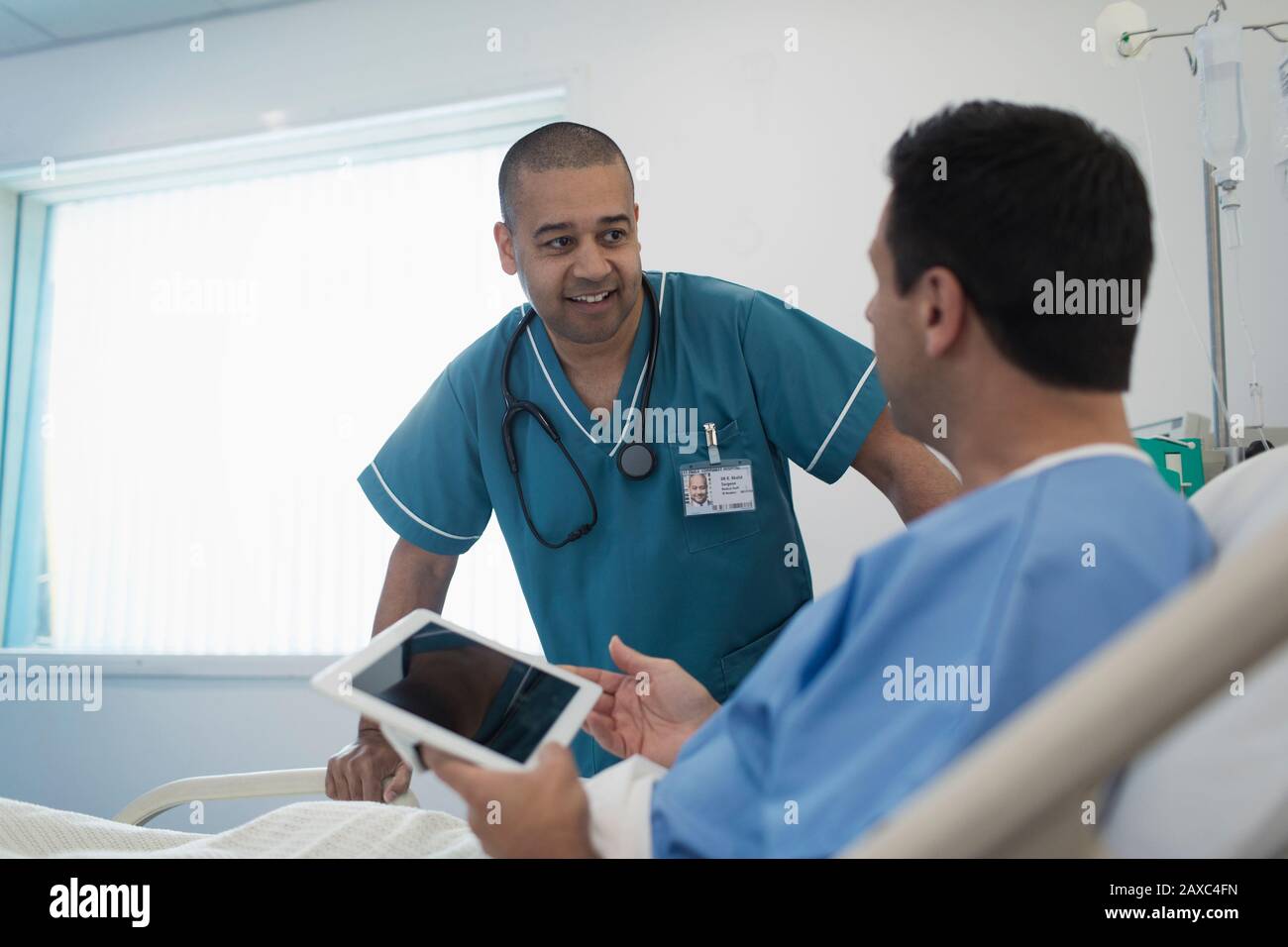 Male nurse talking with patient using digital tablet in hospital bed ...