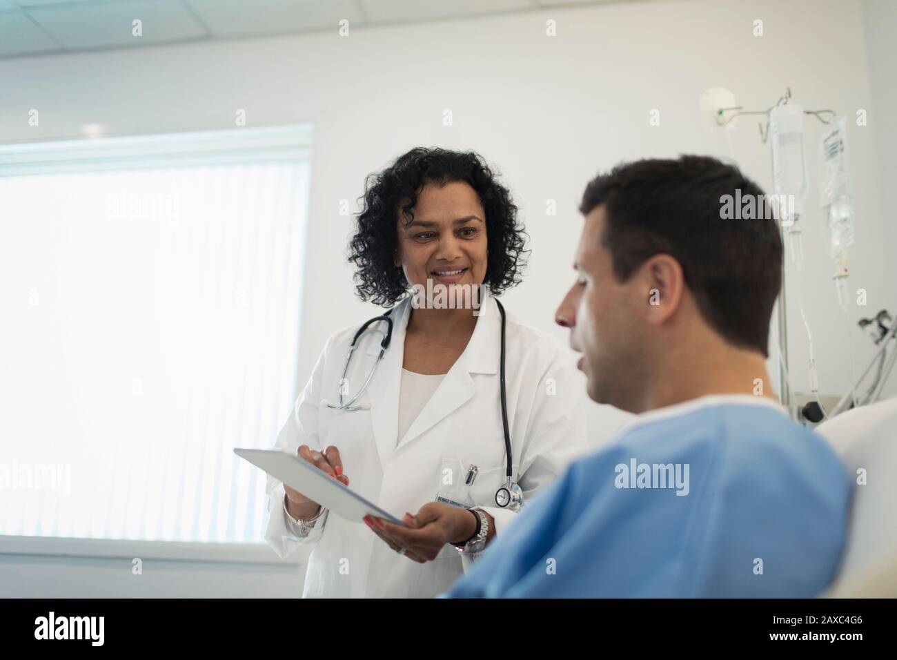 Doctor with digital tablet making rounds, talking with patient in ...
