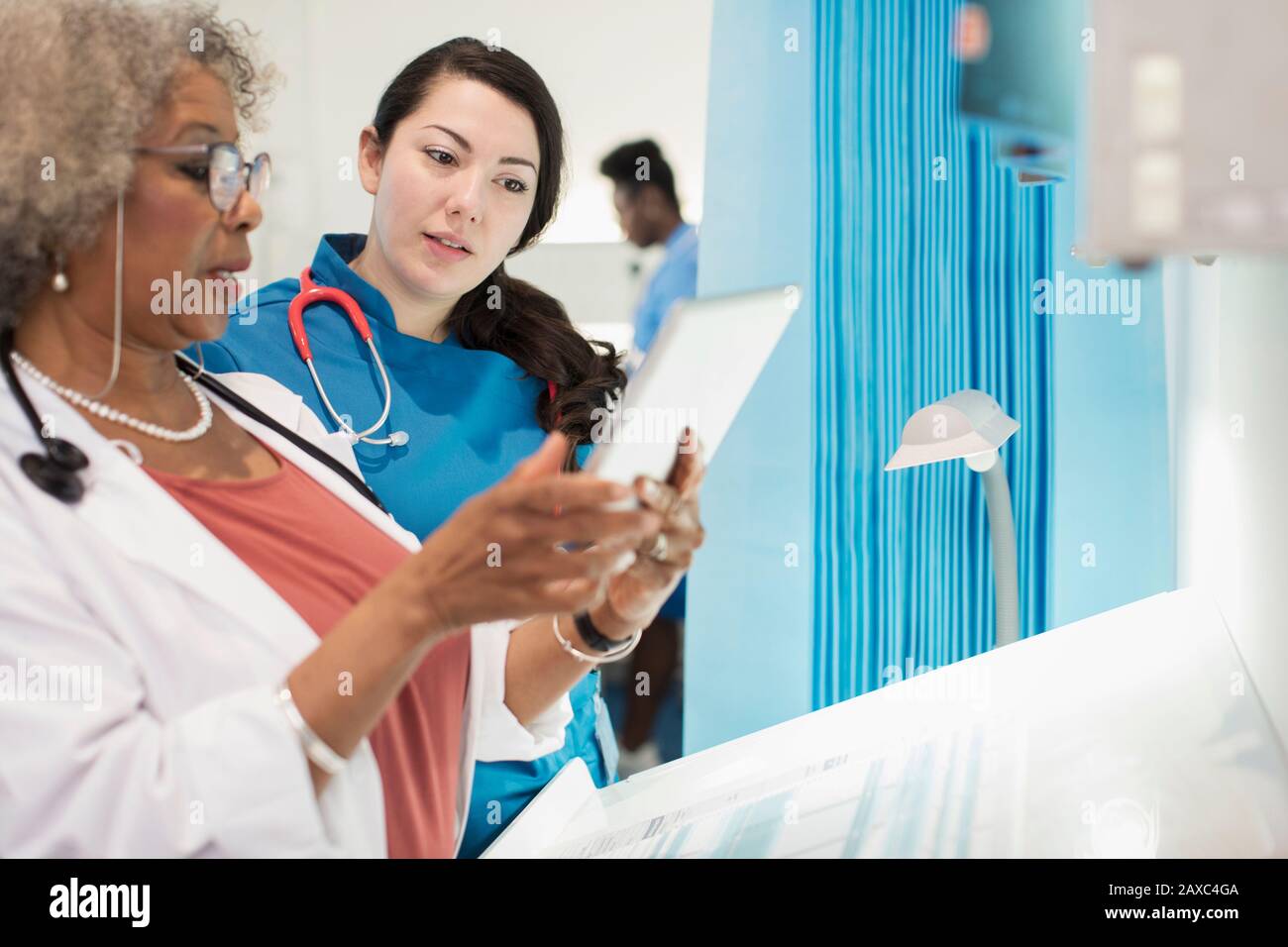 Female doctor and nurse using digital tablet, talking in hospital room ...