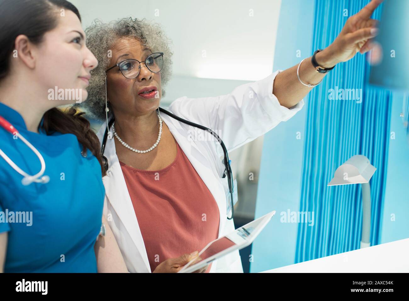 Female doctor and nurse with digital tablet talking in hospital room ...