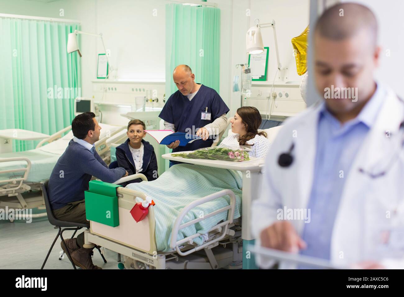 Doctor making rounds, talking with patient and family in hospital ward ...