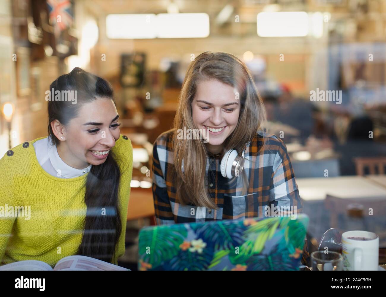 Smiling young women friends using laptop in cafe window Stock Photo - Alamy