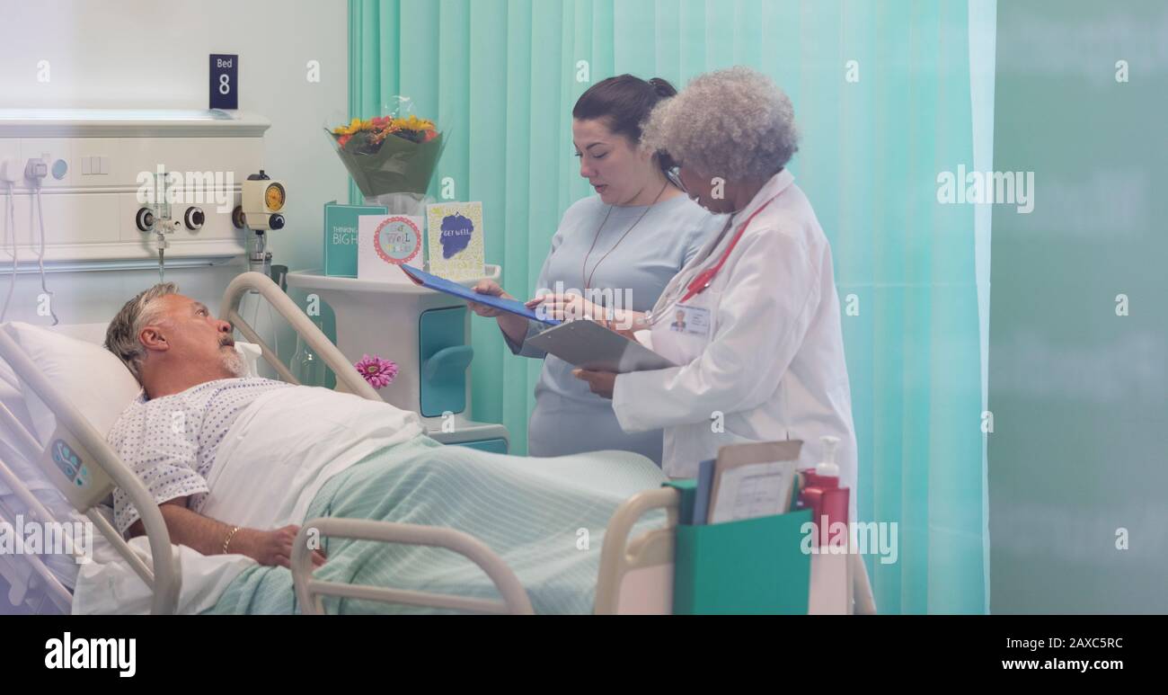 Doctors with medical chart making rounds, talking with senior patient ...