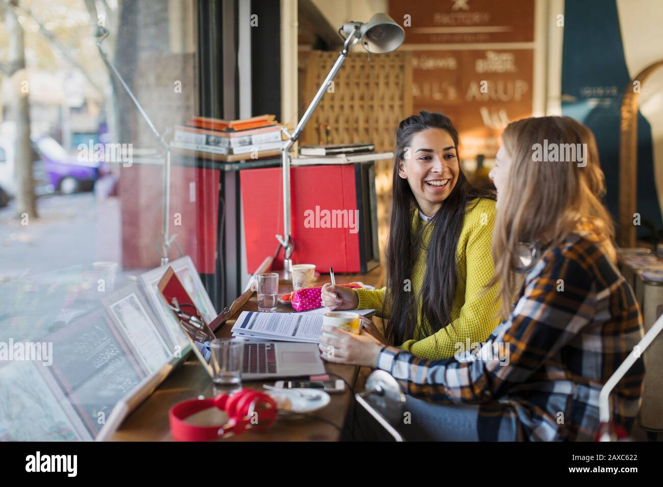 Smiling female college students studying at cafe window Stock Photo - Alamy