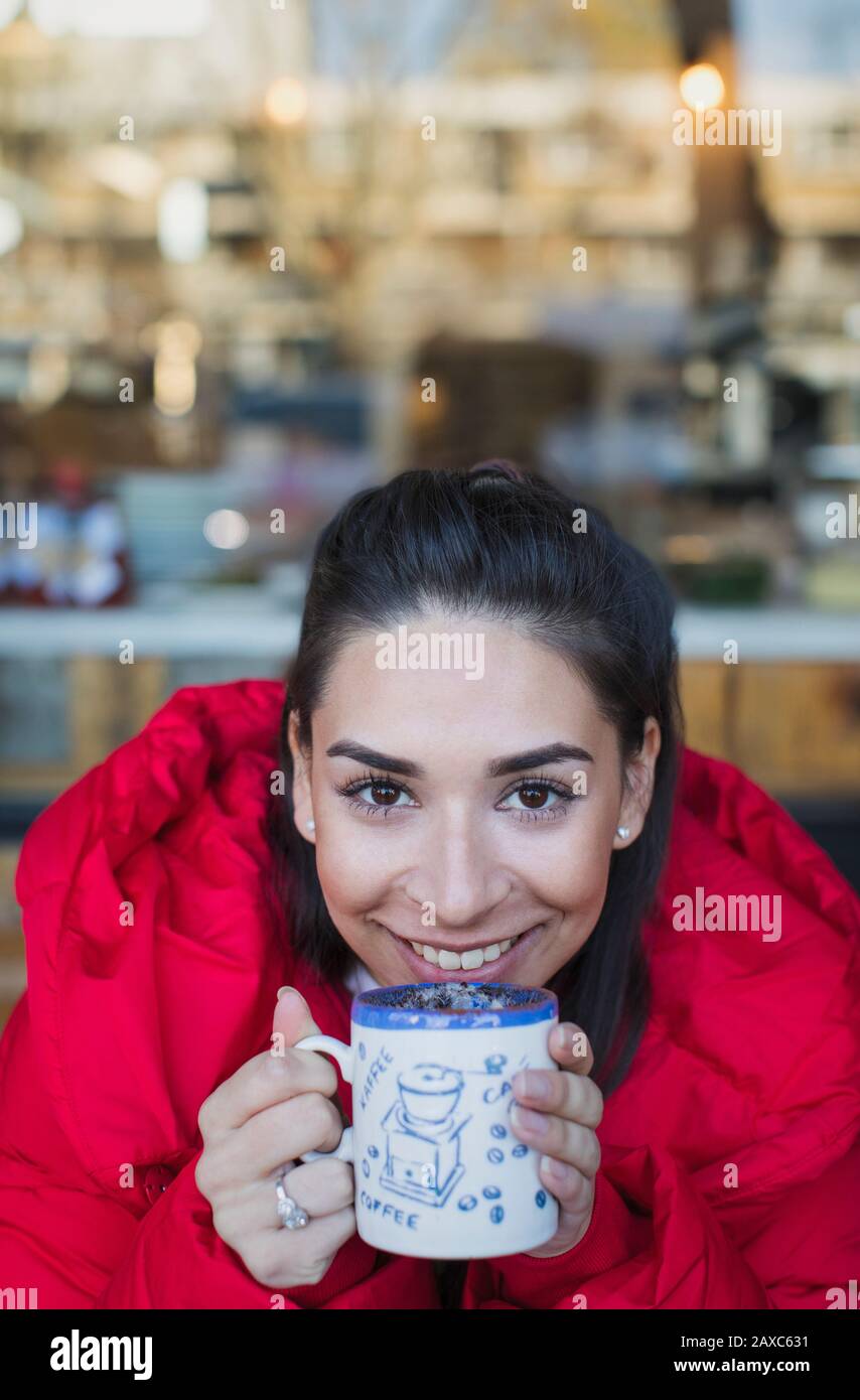 Portrait smiling, confident young woman drinking coffee in cafe window ... Portrait smiling, confident young woman drinking coffee in cafe window ...