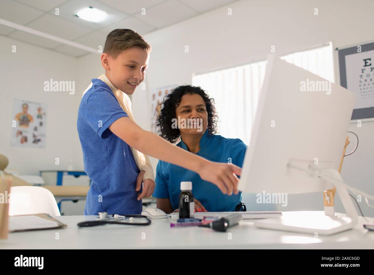 Female pediatrician and boy patient using computer in doctors office ...